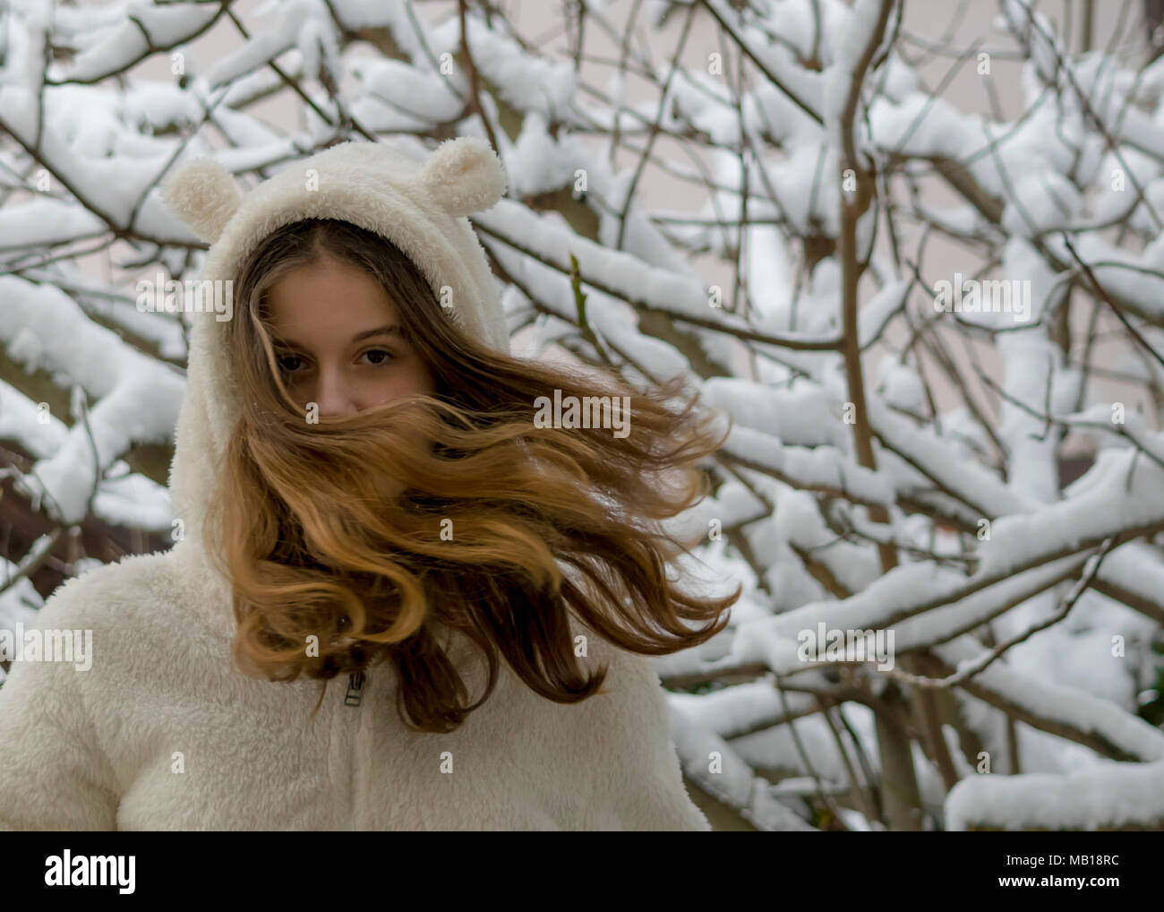 Portrait of beautiful teenage girl in snow. Long hair blows in wind ...