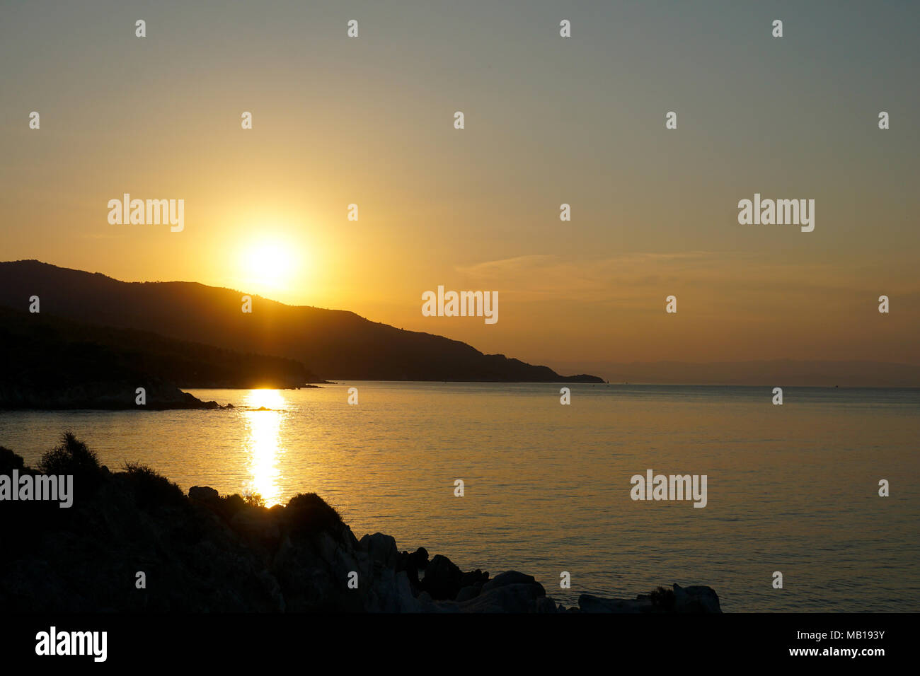Sunset at the sea. Sun falling down behind mountain Stock Photo - Alamy