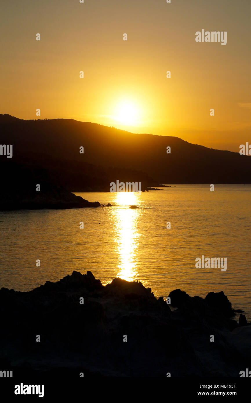 Sunset at the sea. Sun falling down behind mountain Stock Photo - Alamy