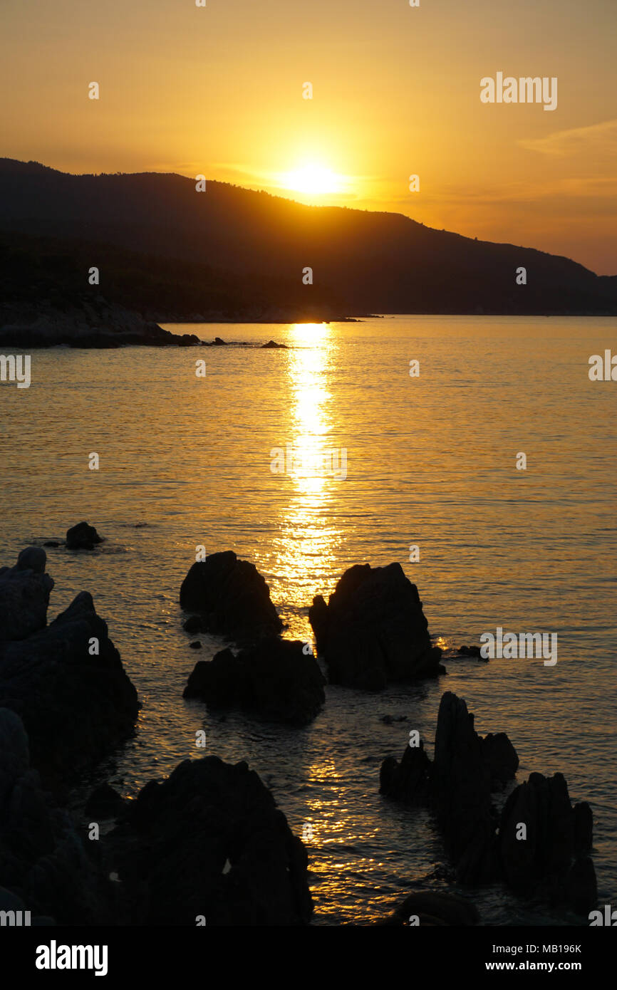 Sunset at the sea. Sun falling down behind mountain Stock Photo - Alamy