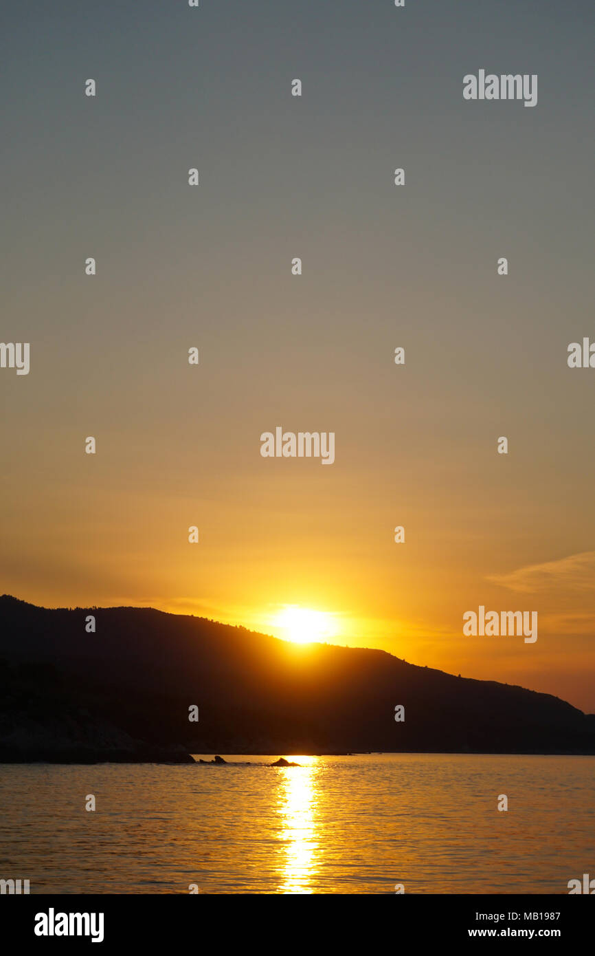 Sunset at the sea. Sun falling down behind mountain Stock Photo - Alamy