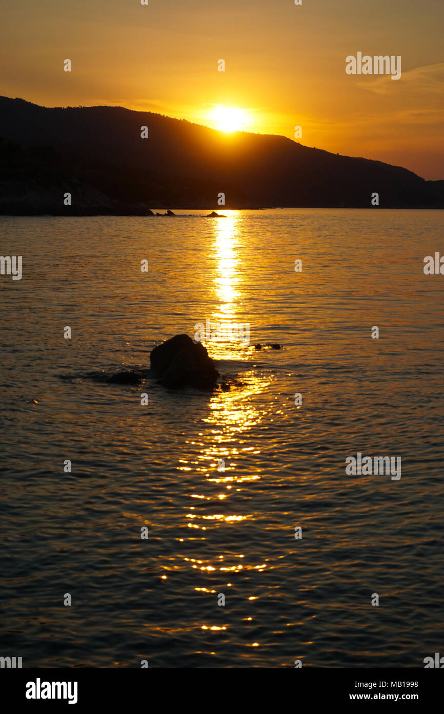 Sunset at the sea. Sun falling down behind mountain Stock Photo - Alamy