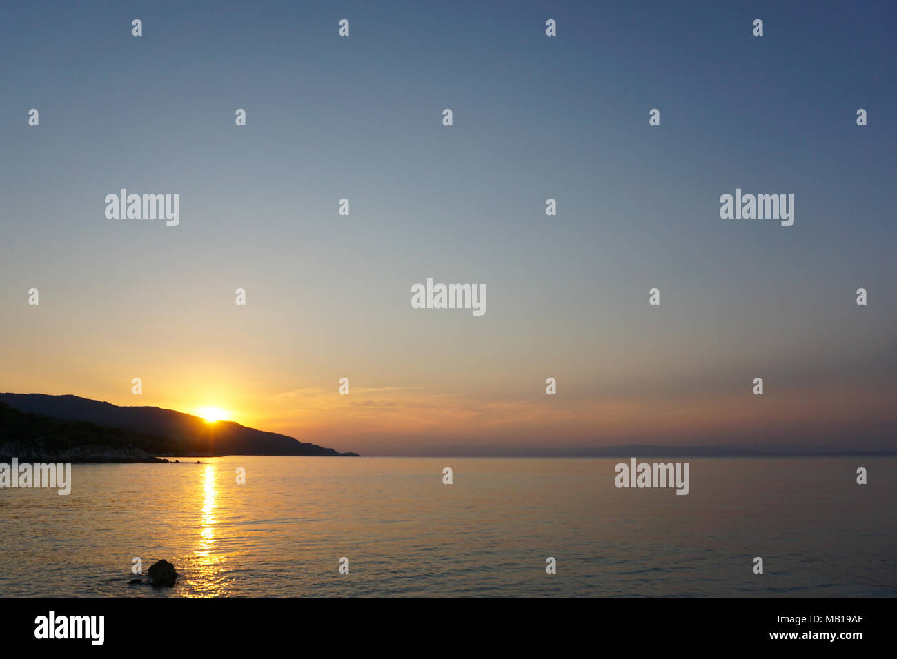 Sunset at the sea. Sun falling down behind mountain Stock Photo - Alamy