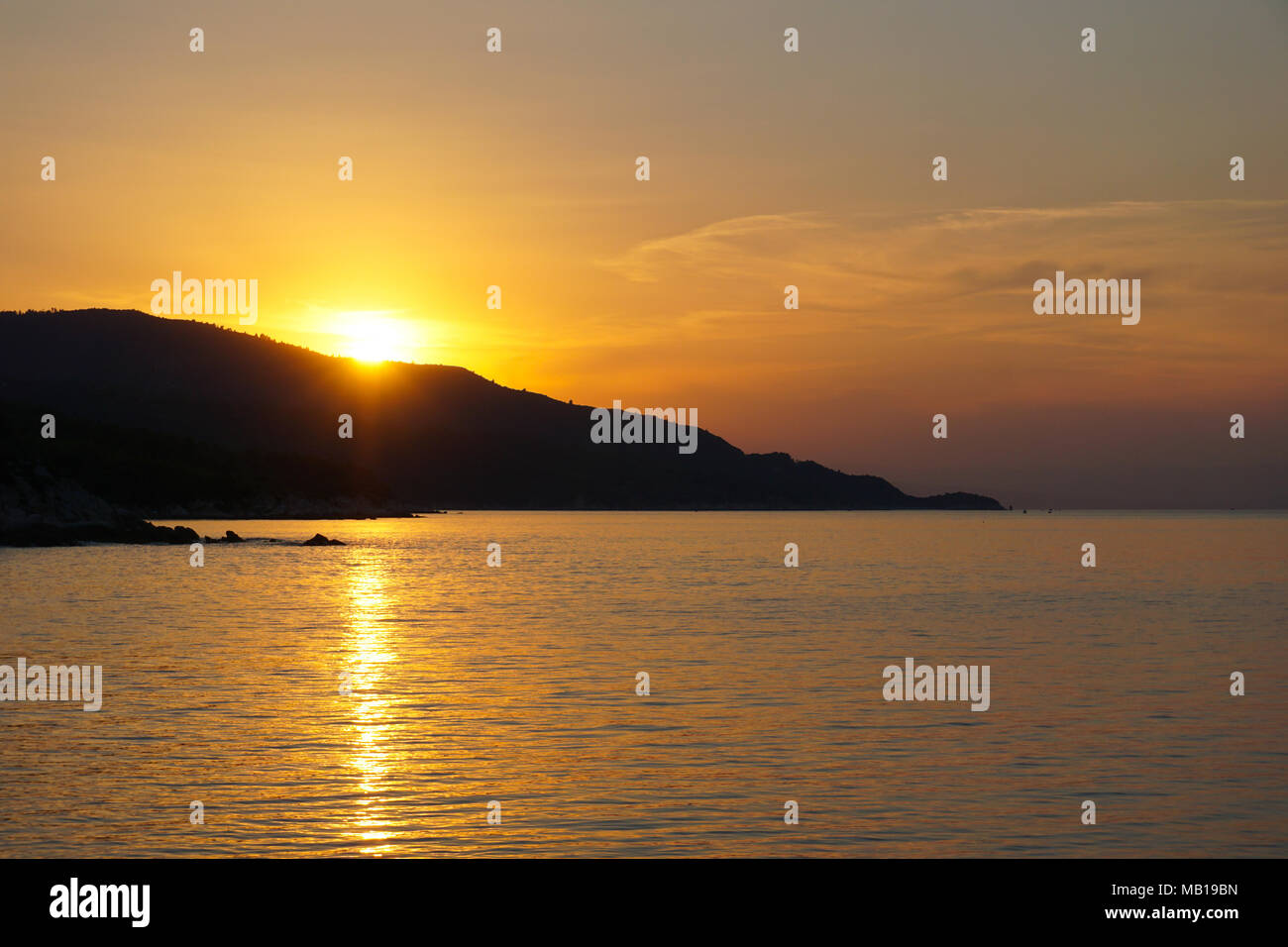 Sunset at the sea. Sun falling down behind mountain Stock Photo - Alamy