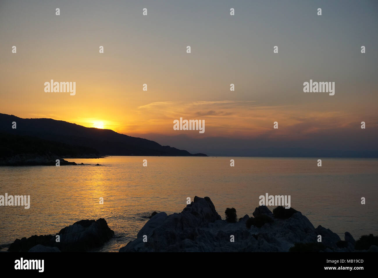 Sunset at the sea. Sun falling down behind mountain Stock Photo - Alamy