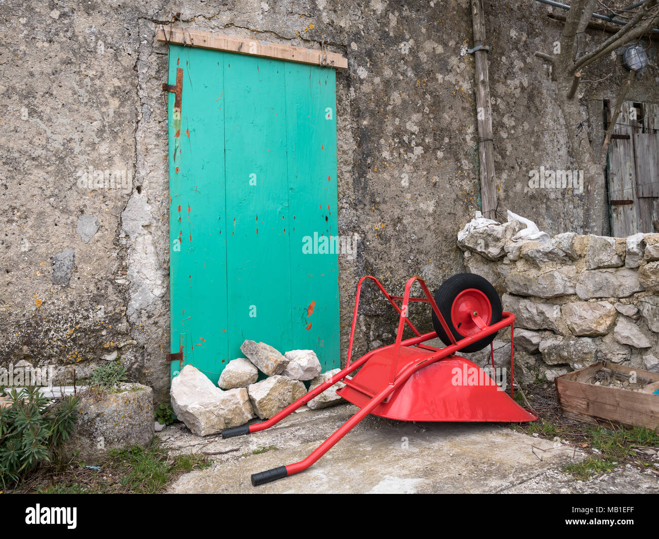 Red wheelbarrow lying on the floor in front of a green door of an old ...