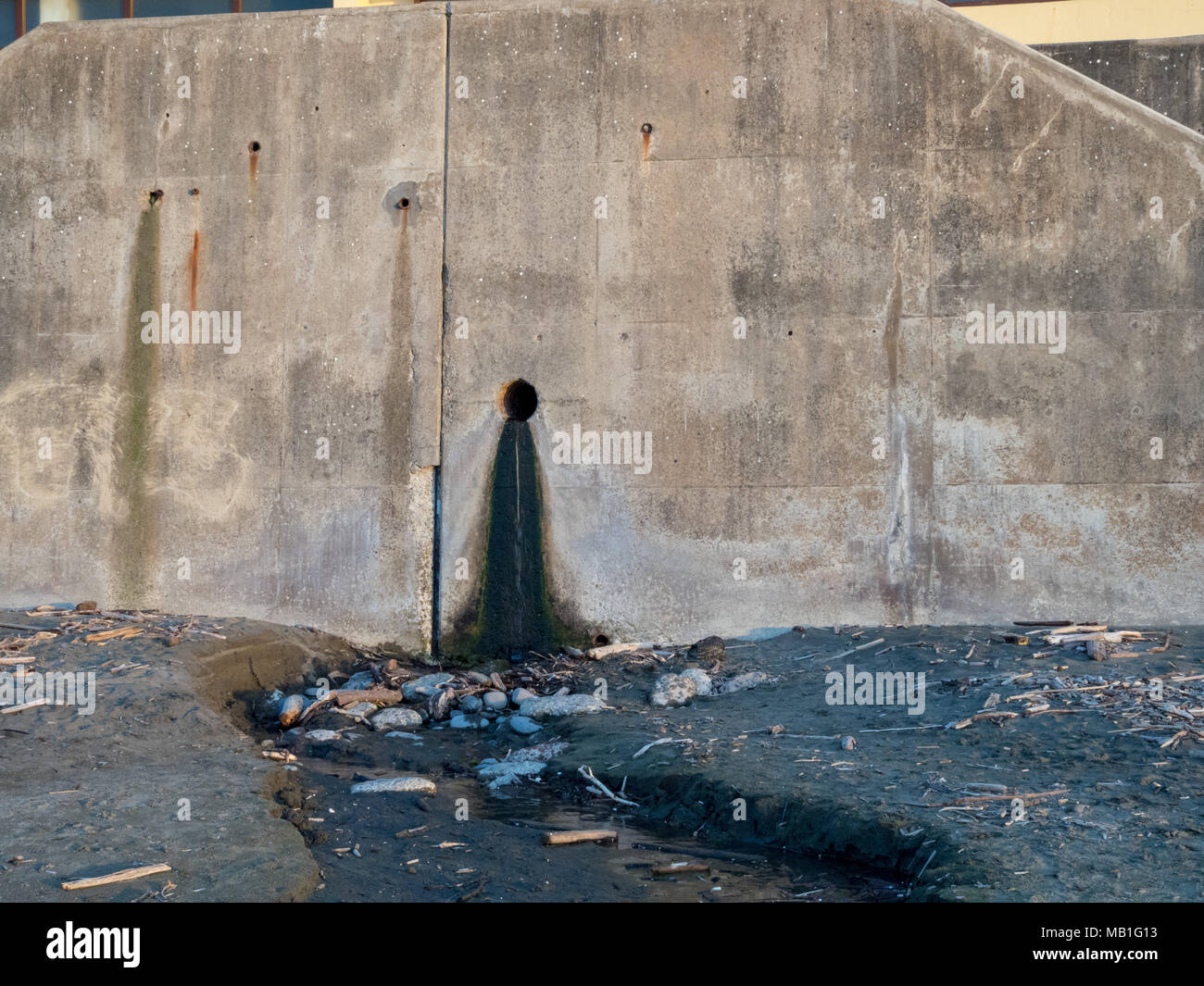 Stained hole in wall releasing dam water onto the beach Stock Photo - Alamy