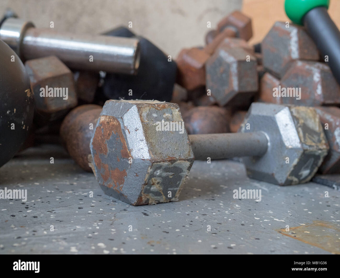 Peeling, rusty dumbbell sitting near stack of other weights on gym ...