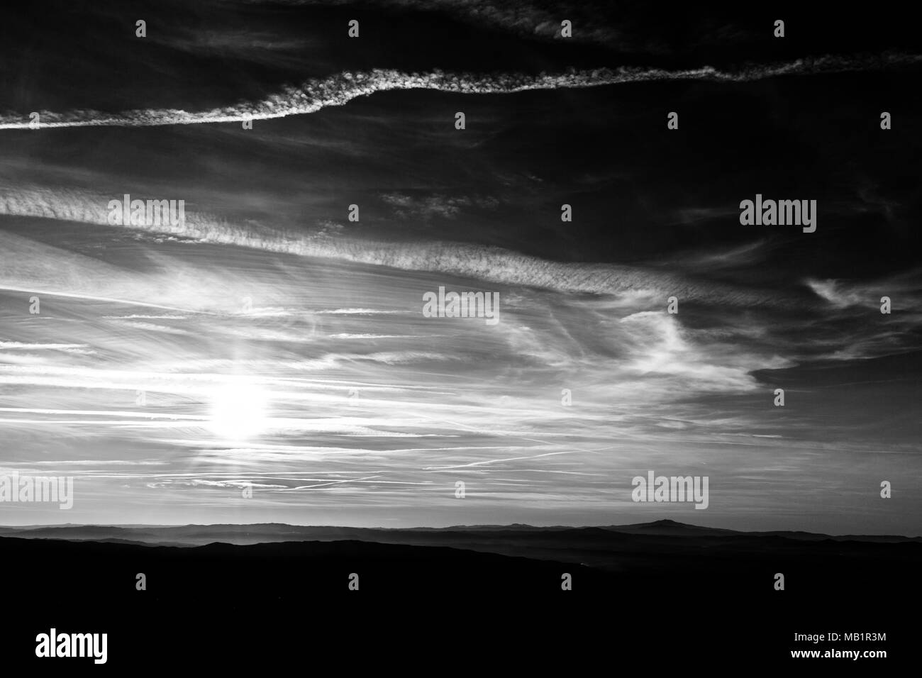 Sunset over distant mountains, with deep sky full of white clouds and ...