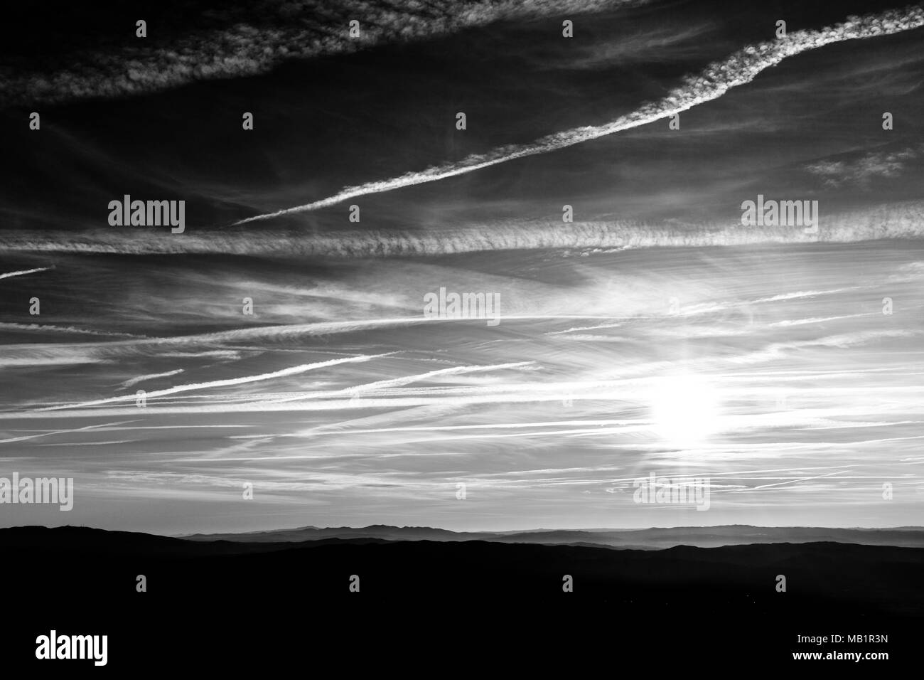 Sunset over distant mountains, with deep sky full of white clouds and ...