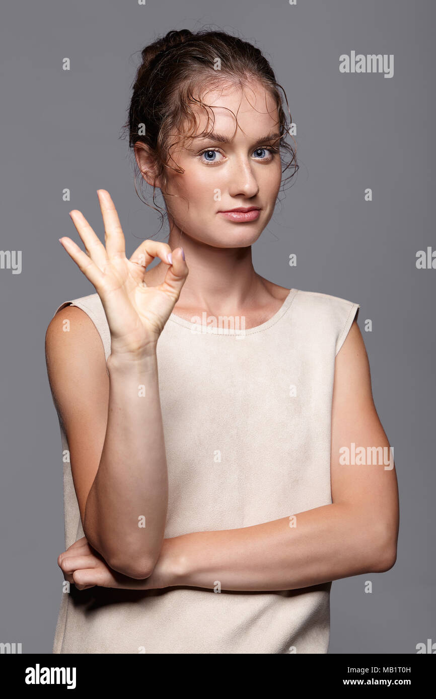 Young woman making OK sign. Beautiful female in dress on gray ...
