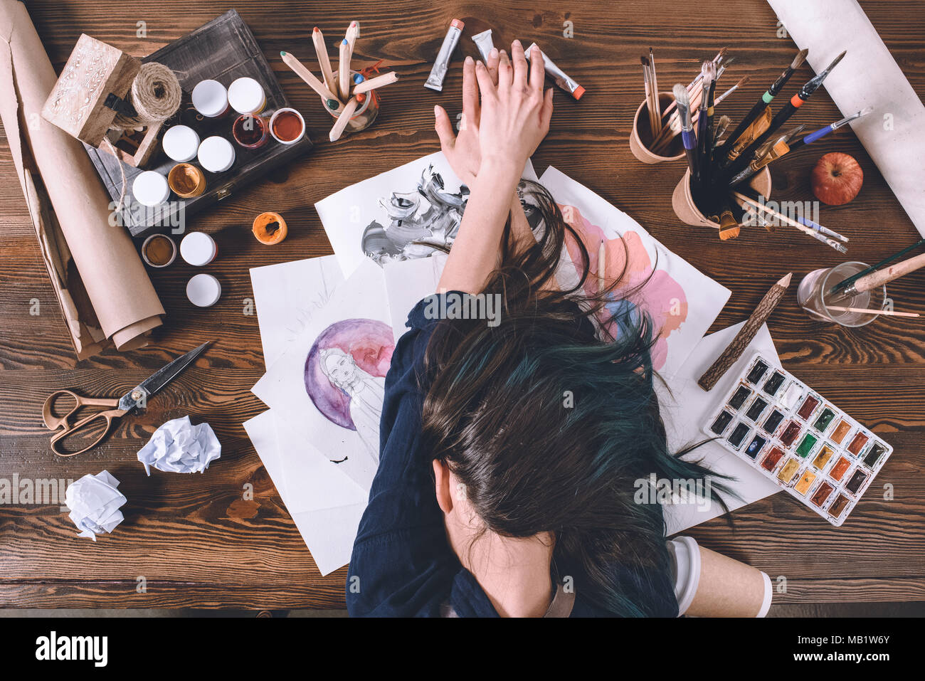 top view of female artist sleeping on sketches and paints at workplace ...