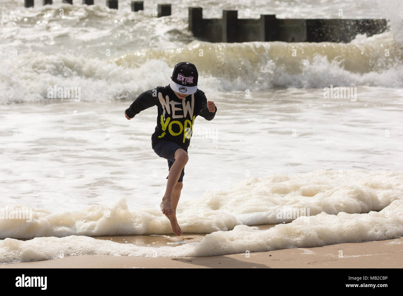 Boy running out of the sea through foam created by the waves, Boscombe ...