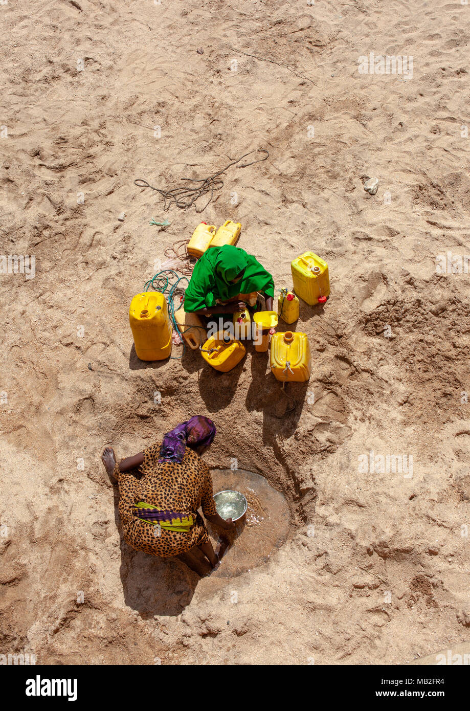 Somali women taking drinking water from a well hole in the sand and ...