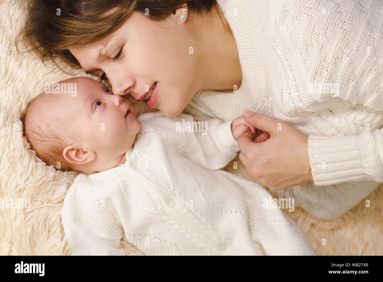Mother and newborn daughter lie on pink plaid. They are dressed in warm ...