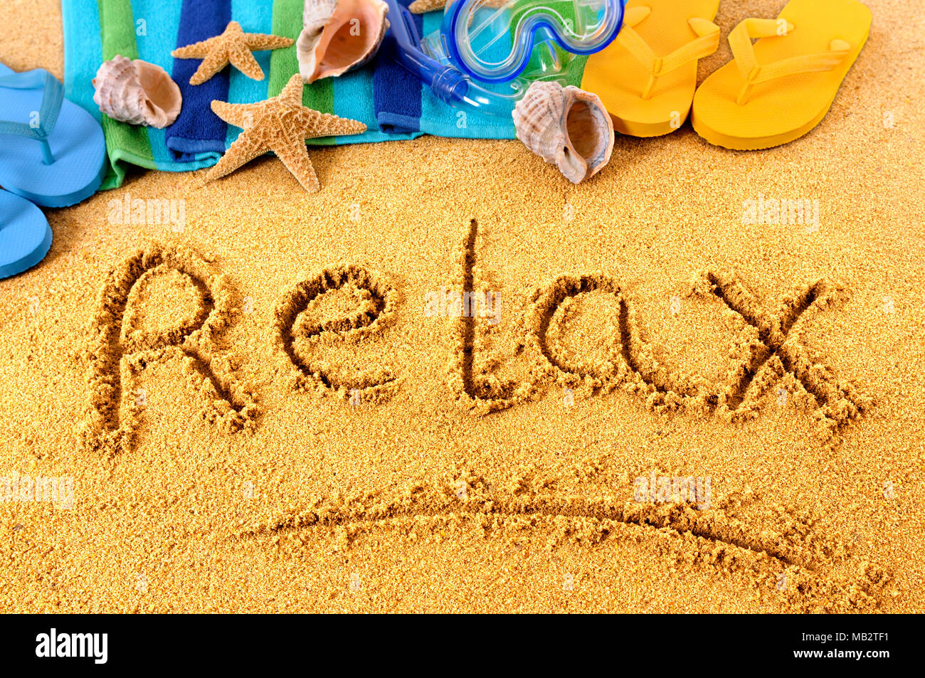 The word Relax written on a sandy beach, with scuba mask, beach towel ...