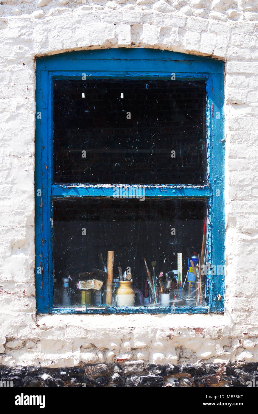 A blue-framed window in a white painted wall, with artist's materials ...
