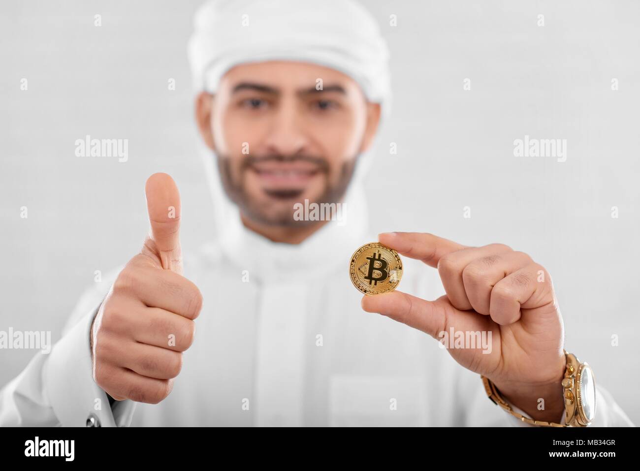 Young Muslim trader keeps golden coin on the white studio background. A ...