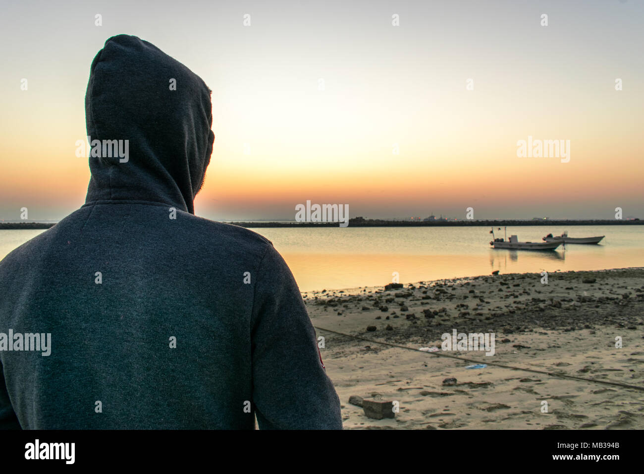 closeup of a man looking to the sunset at a beach and sea boats in the ...