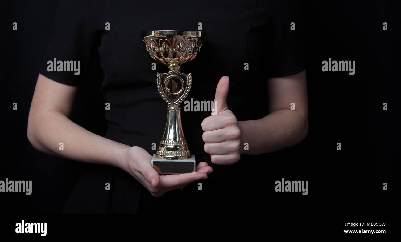 low key image of a woman holding a trophy cup over dark background ...