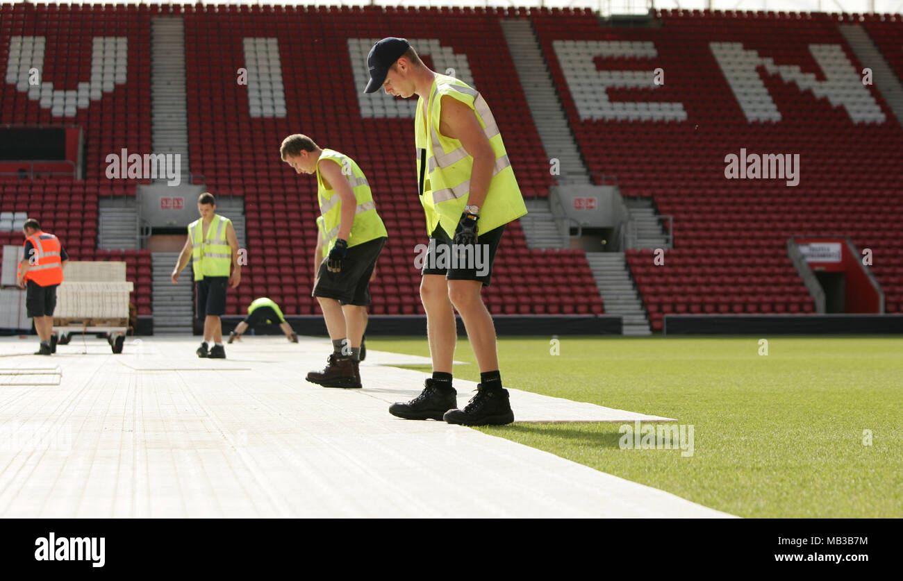 Workers lay a temporary plastic flooring over a football pitch to ...