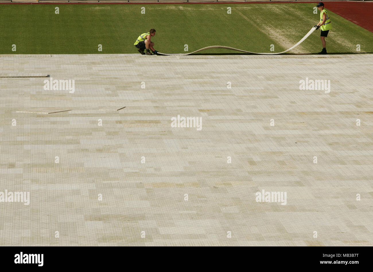 Workers cover the grass of a football stadium pitch with plastic ...