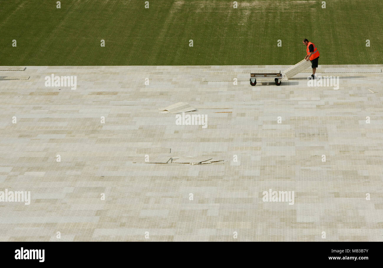 Workers cover the grass of a football stadium pitch with plastic ...