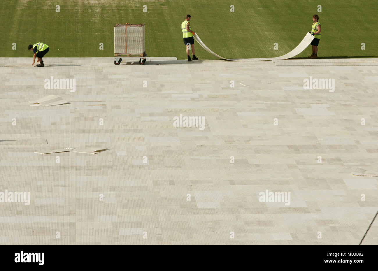 Workers cover the grass of a football stadium pitch with plastic ...