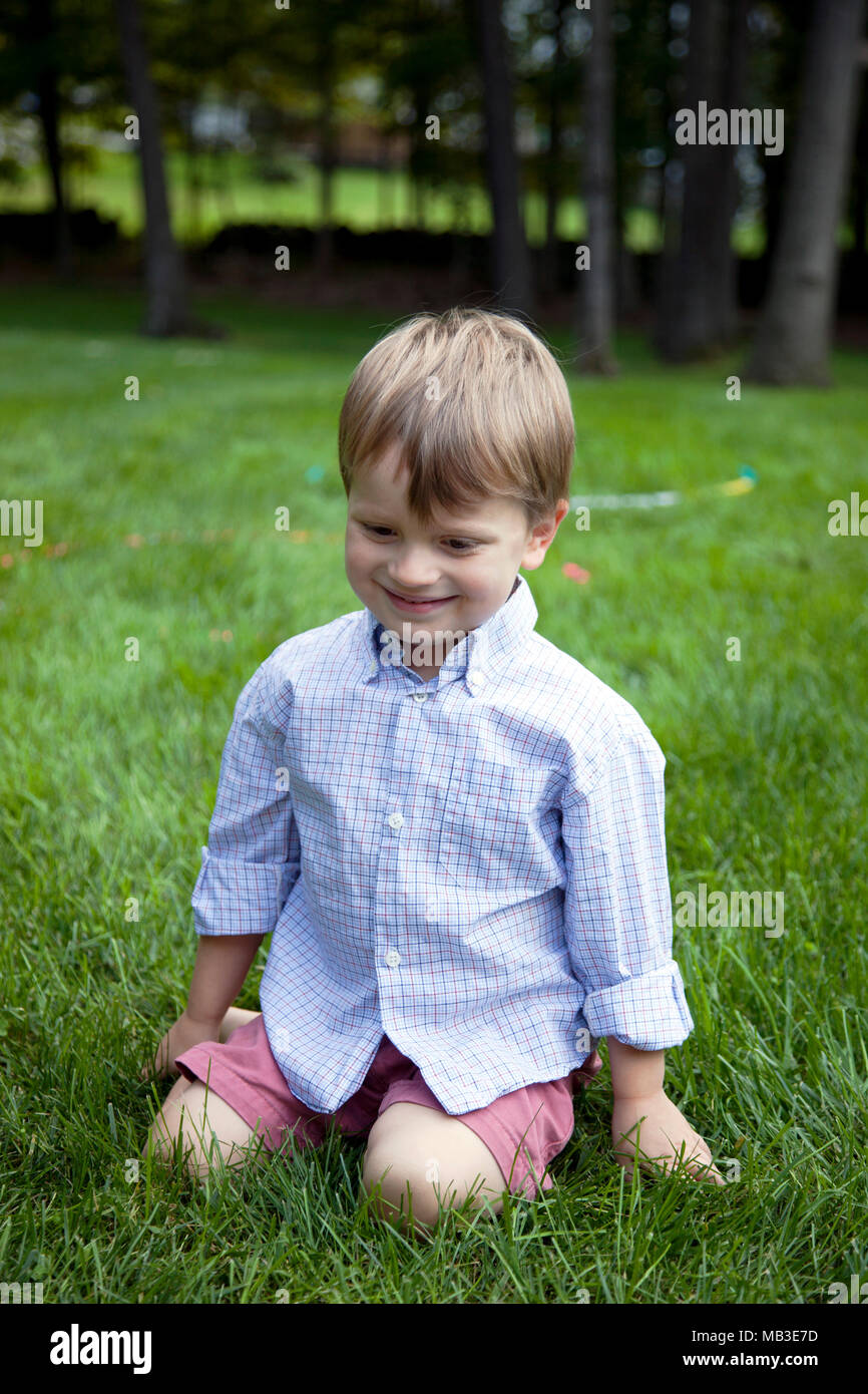 Smiling Young Boy Kneeling in Grass Stock Photo - Alamy