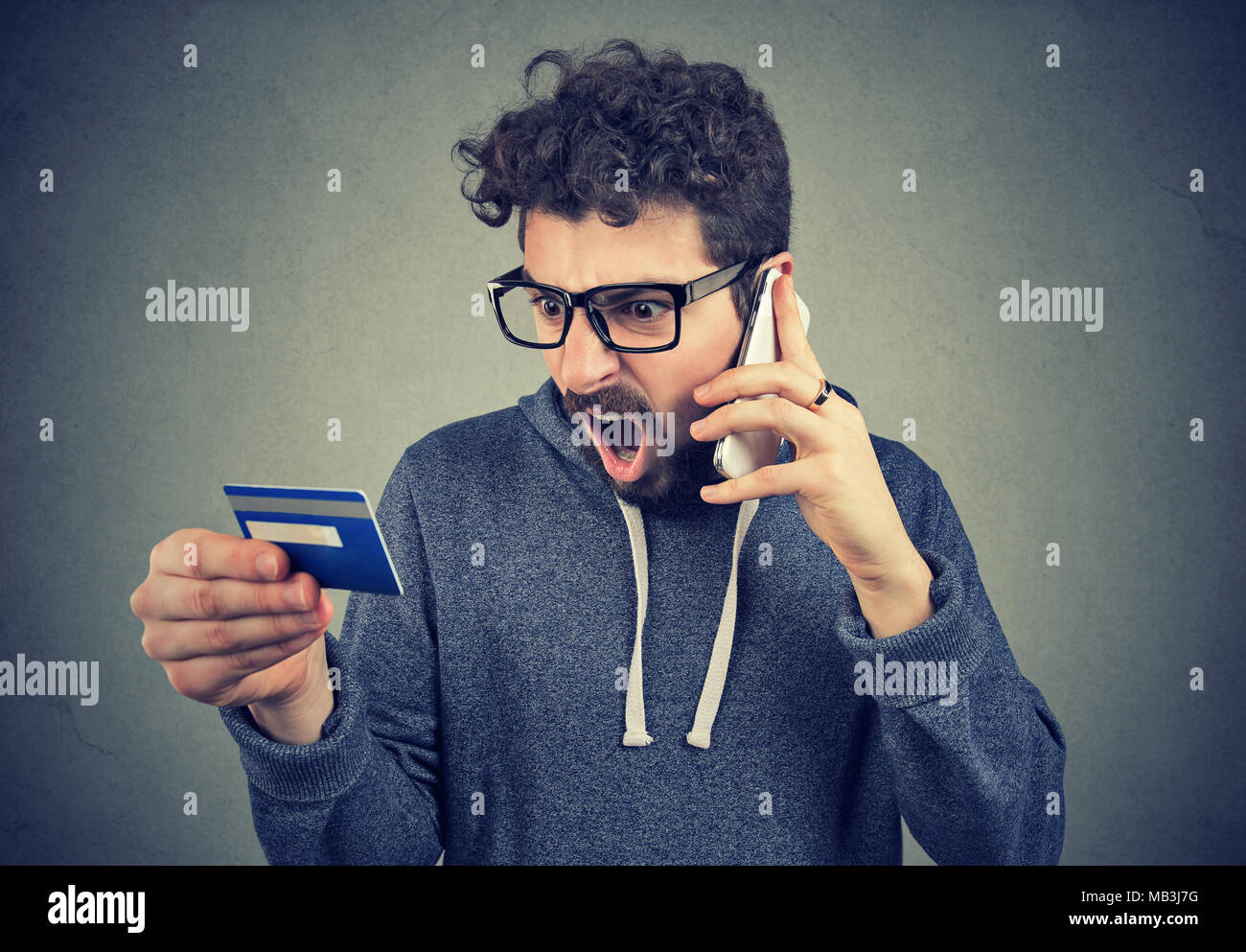 Angry young man talking on the phone while holding credit card and ...