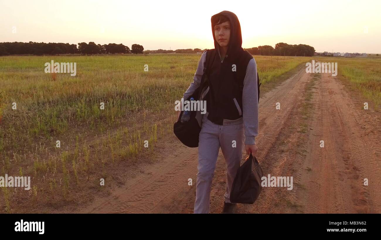 Boy teen traveling. Boy teenage tramp walking along the road in a hood ...
