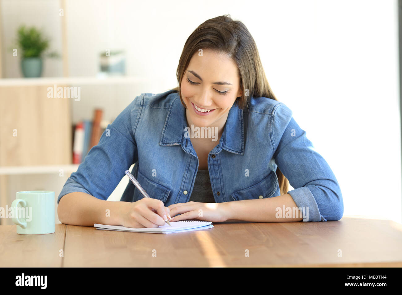 Front view portrait of a happy woman writing in a notebook on a table ...