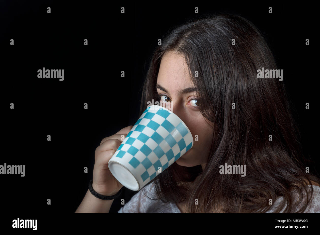 Teenage girl having a cup of tea and looking at camera. On black ...