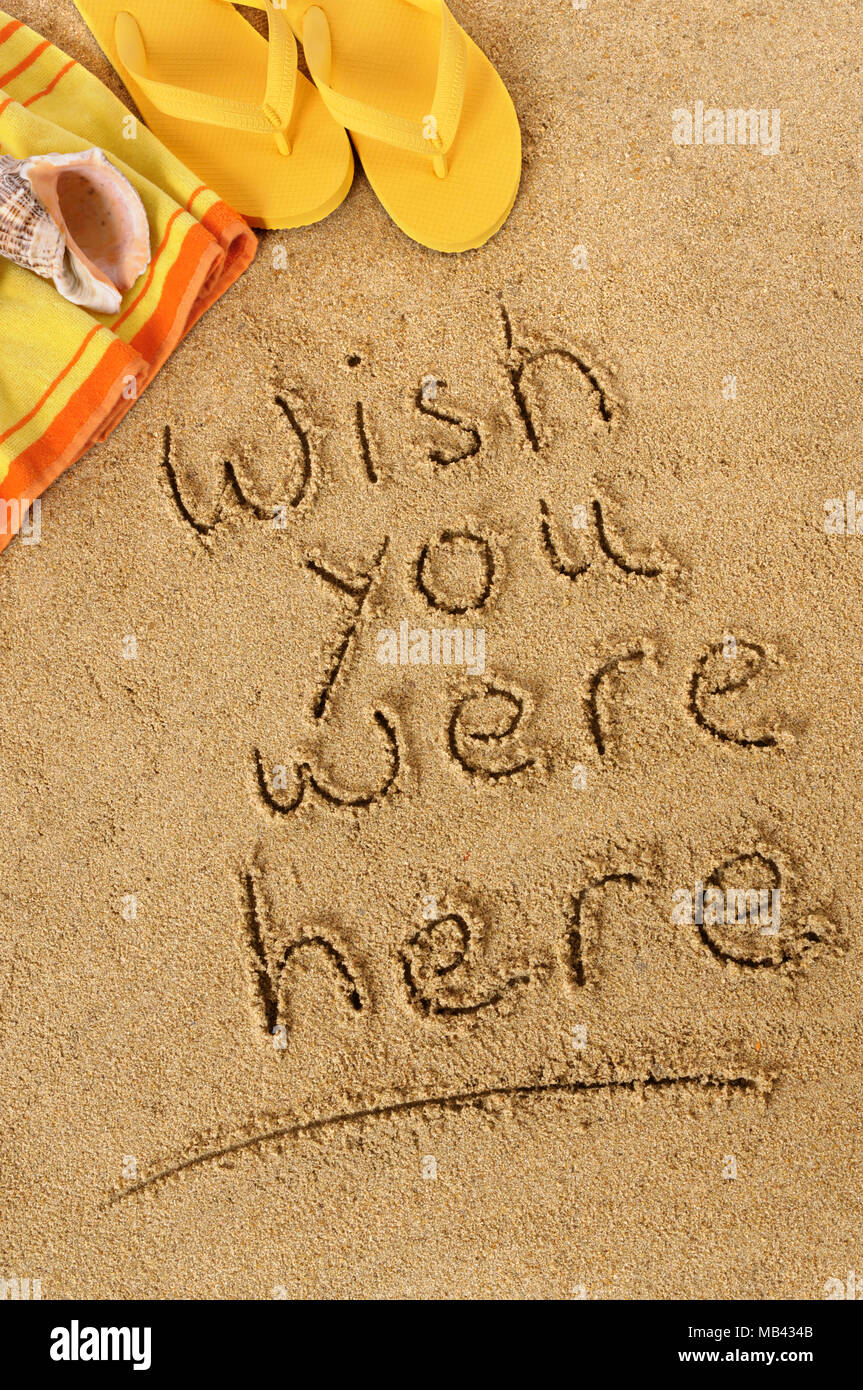 Classic postcard message written in sand with beach towel, seashells ...