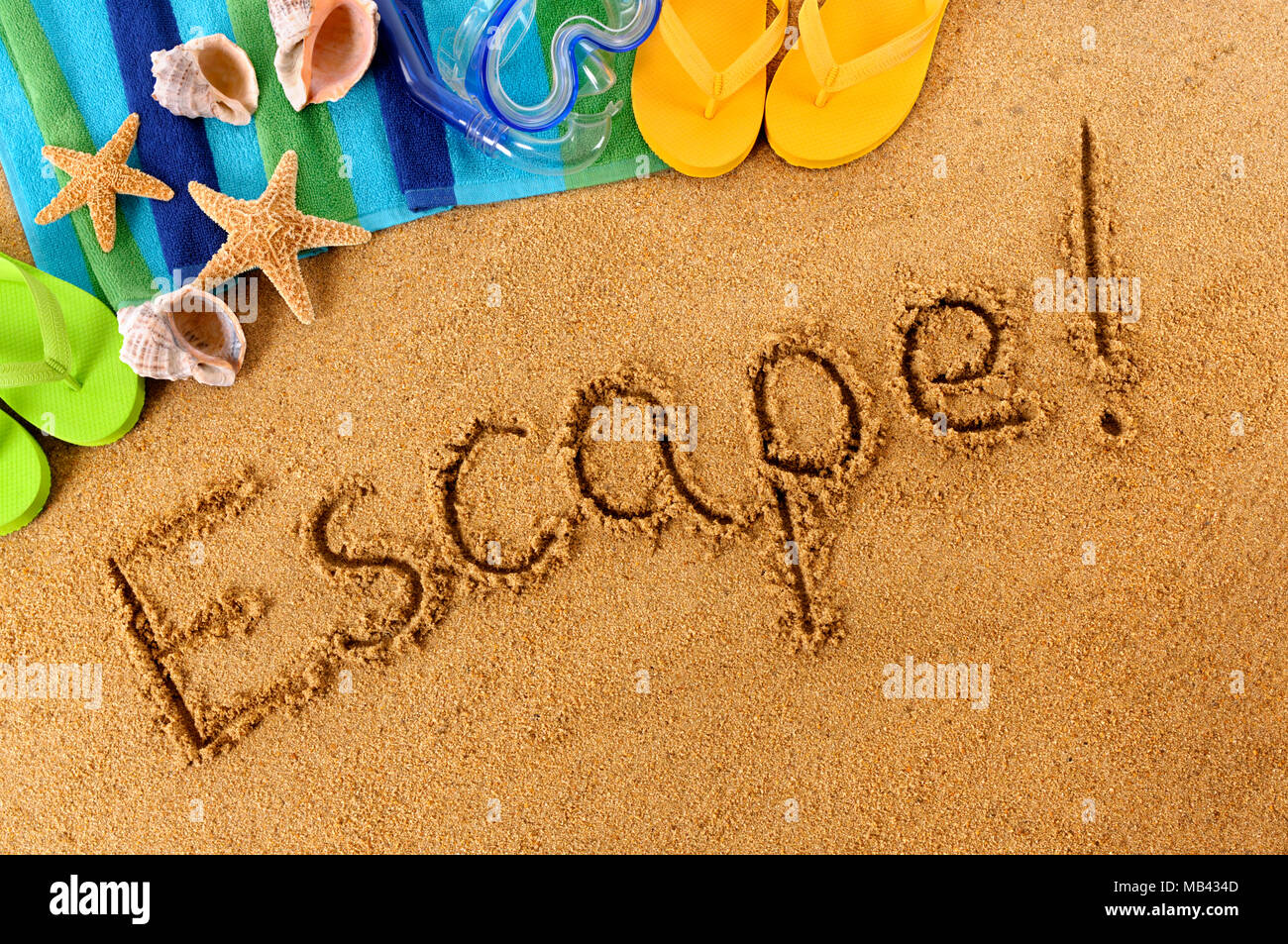 The word Escape! written on a sandy beach, with scuba mask, beach towel ...