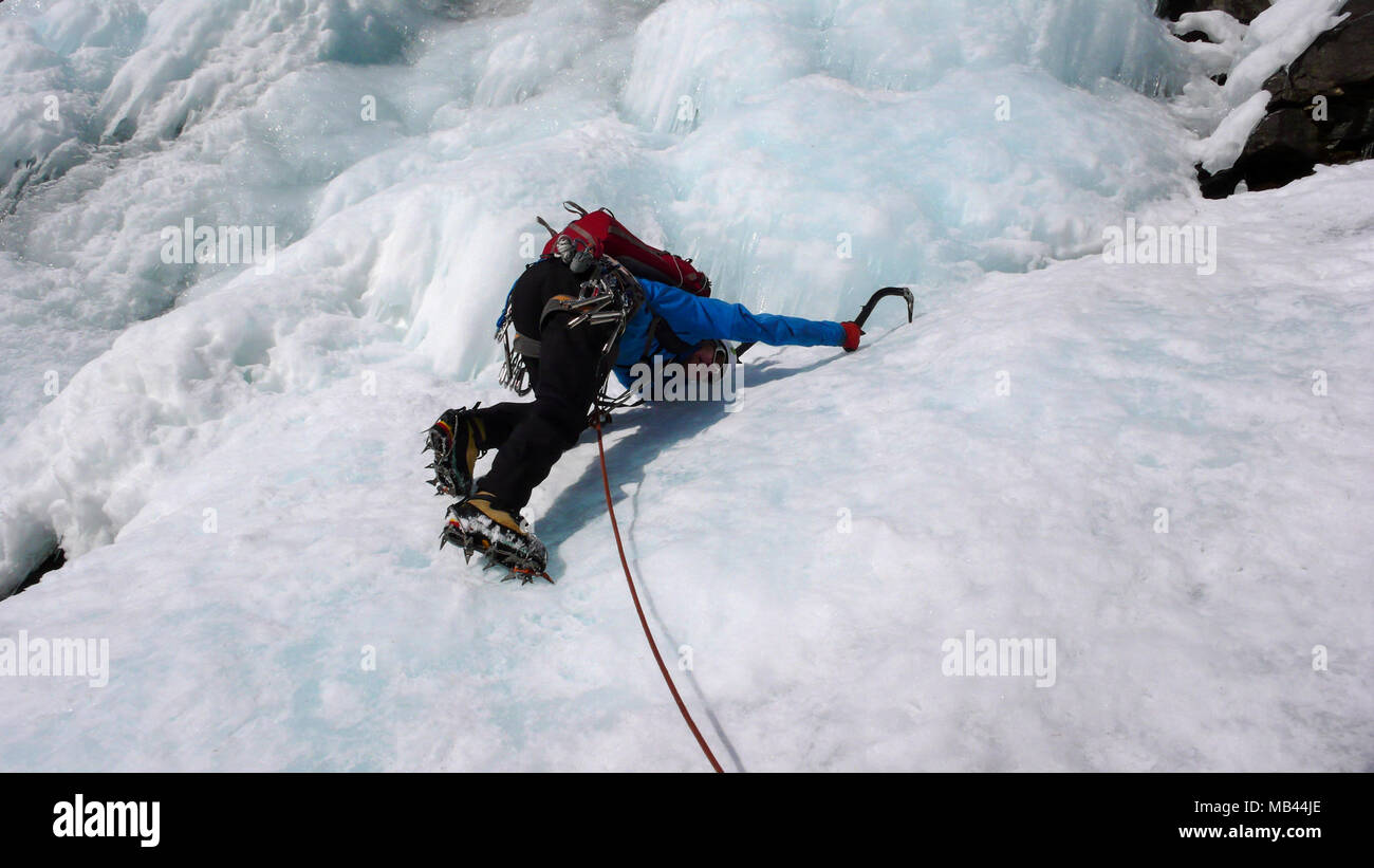 male ice climber in a blue jacket on a gorgeous frozen waterfall ...