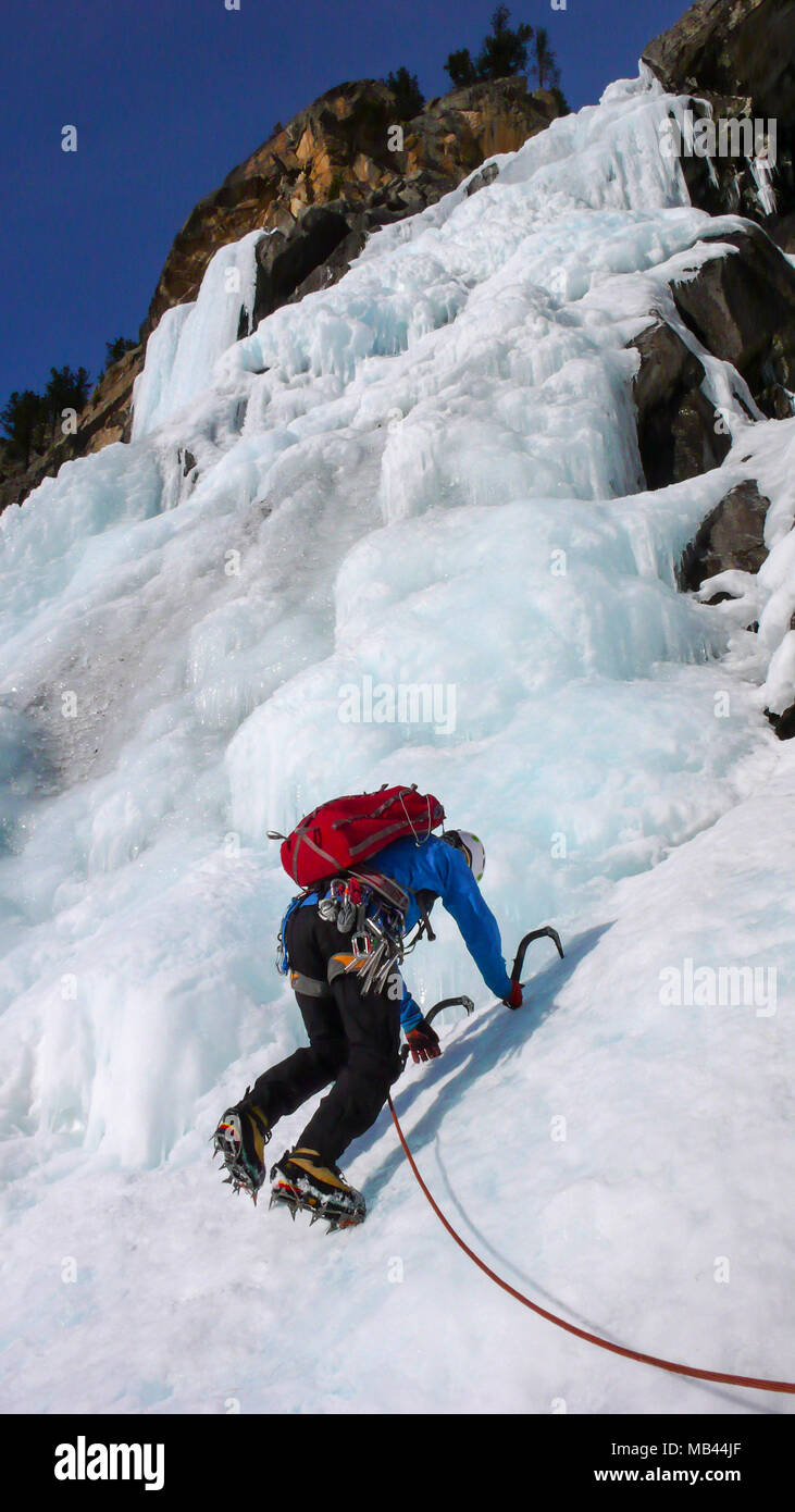 male ice climber in a blue jacket on a gorgeous frozen waterfall ...