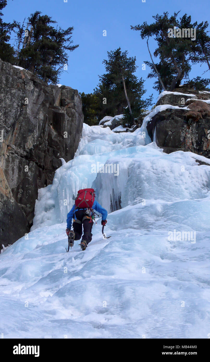 male ice climber in a blue jacket on a gorgeous frozen waterfall ...