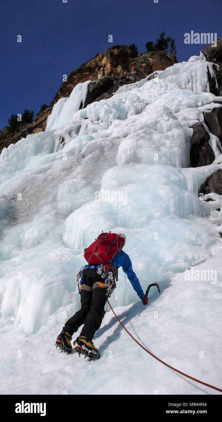 male ice climber in a blue jacket on a gorgeous frozen waterfall ...