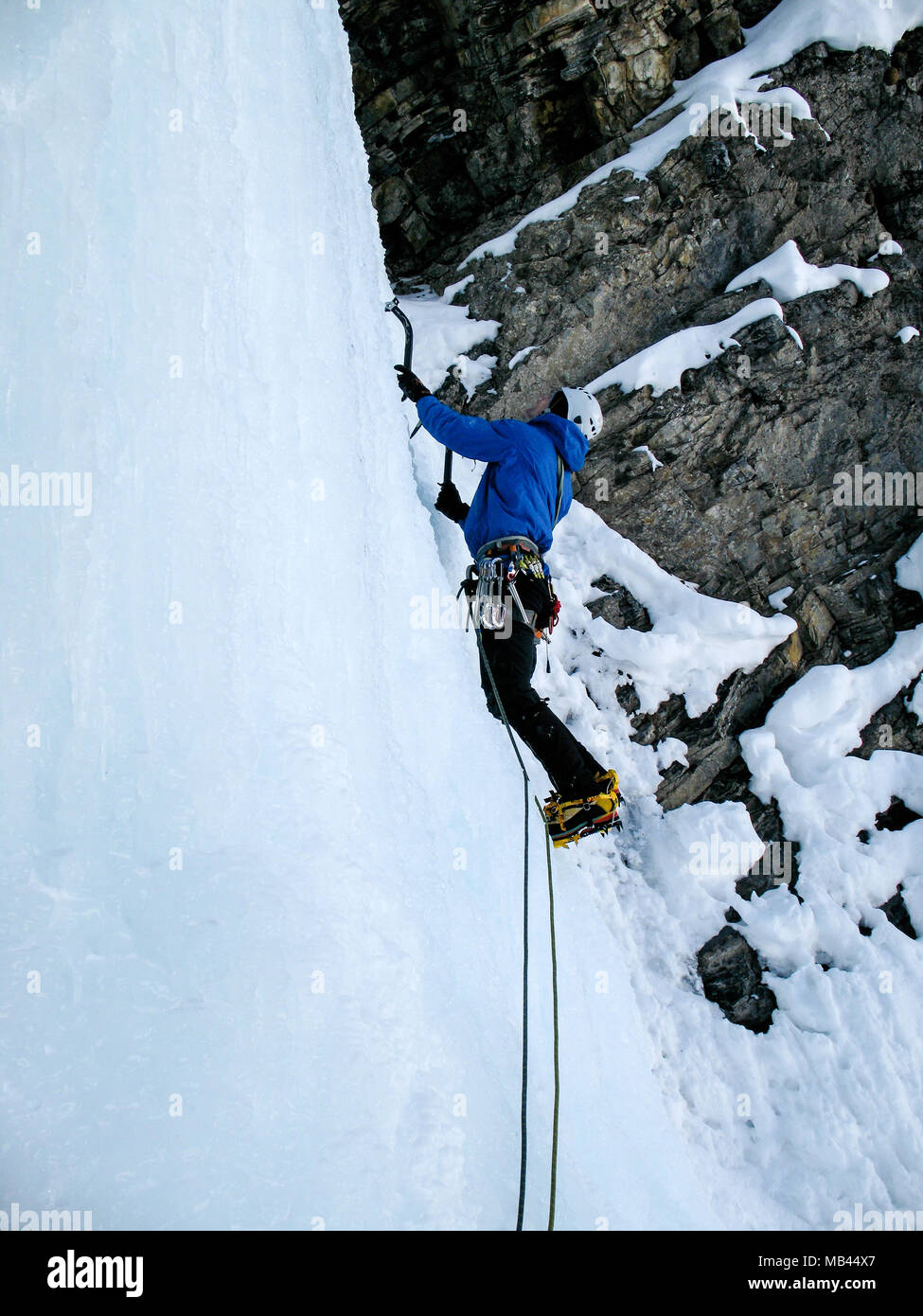 male ice climber lead climbing on a steep waterfall in the Swiss Alps ...