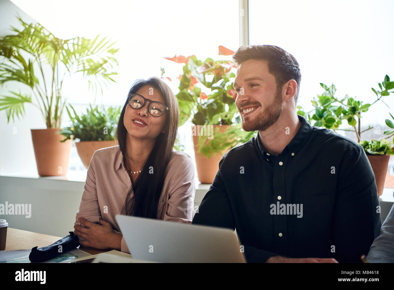 Two smiling work colleagues sitting together at a boardroom table ...