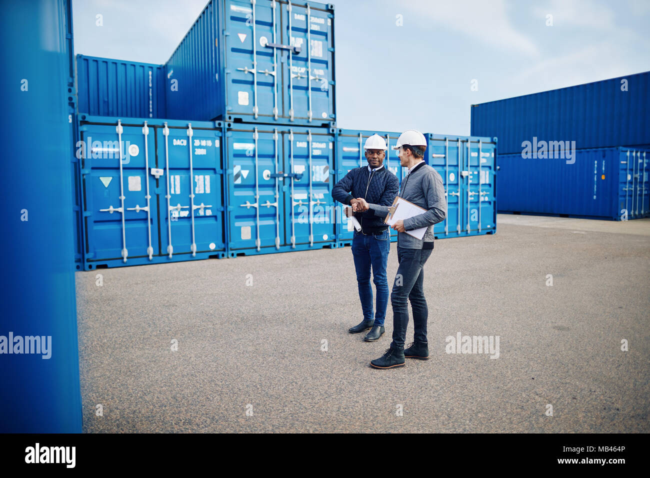 Two smiling engineers wearing hardhats standing by freight containers ...