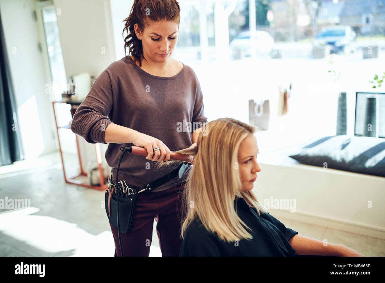 Young stylist styling the hair a female client sitting in a chair with ...