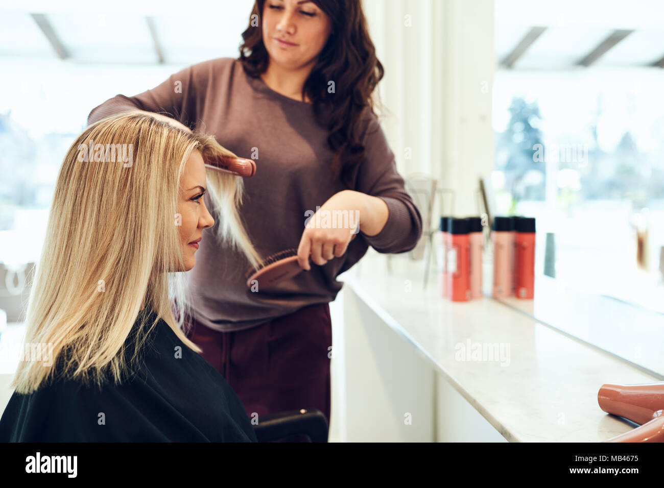 Smiling young woman sitting in a salon chair having her long blonde ...