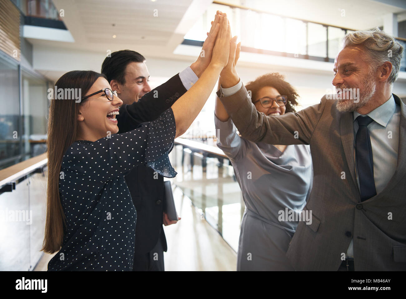 Diverse group of smiling work colleagues high fiving each other while standing together in a ...