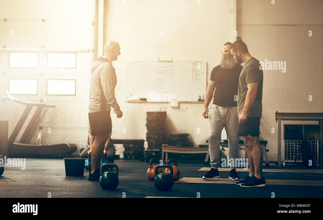 Three fit men in sportswear smiling and talking together around weights ...