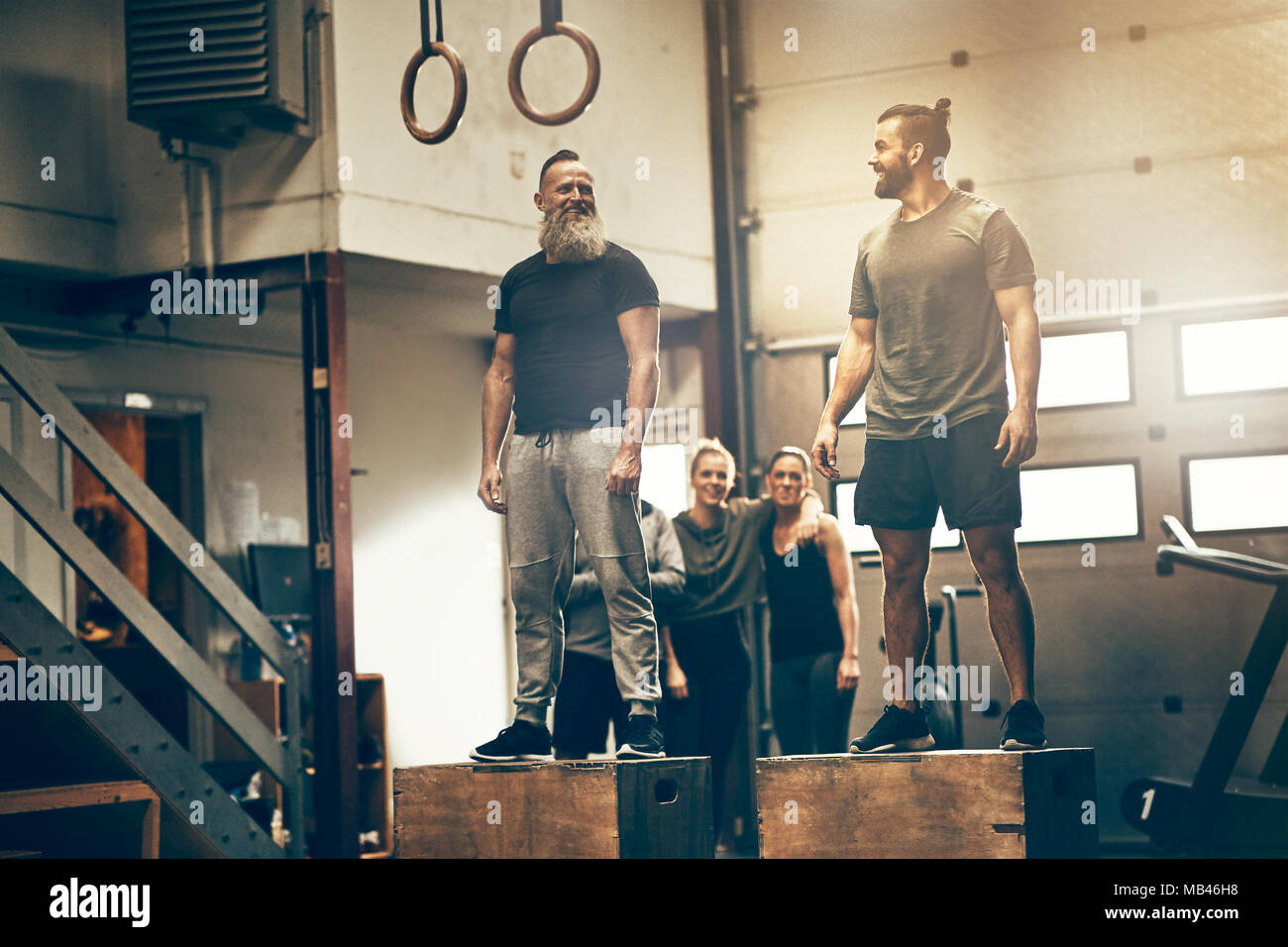 Two fit men standing on boxes during a gym workout session with friends ...