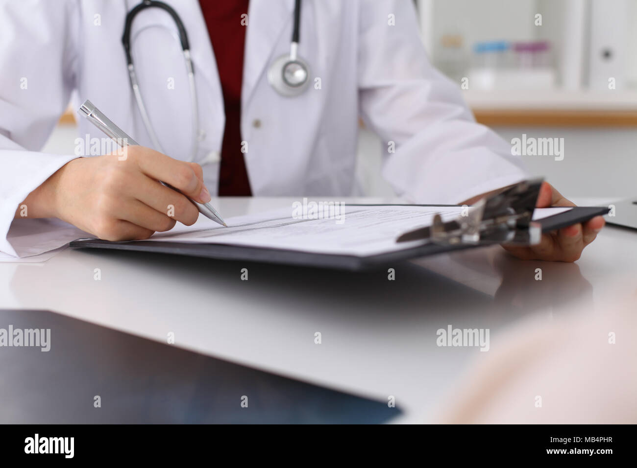 Close up of a female doctor filling up an application form while ...