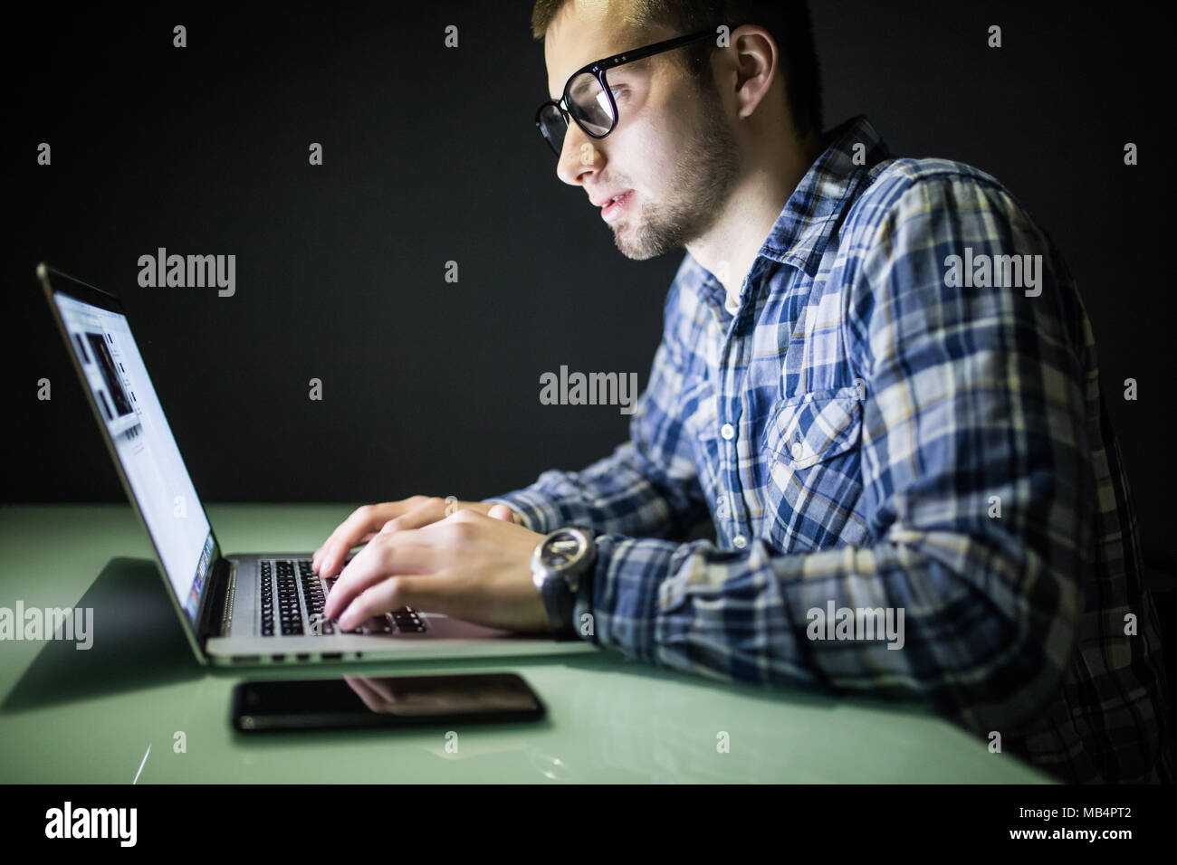 Young man working on computer at night in dark office. The designer ...