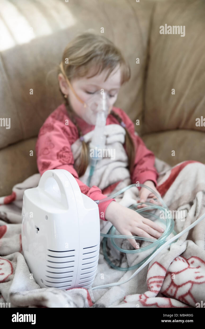 Little girl in a mask treats a runny nose using a nebulizer, at home ...